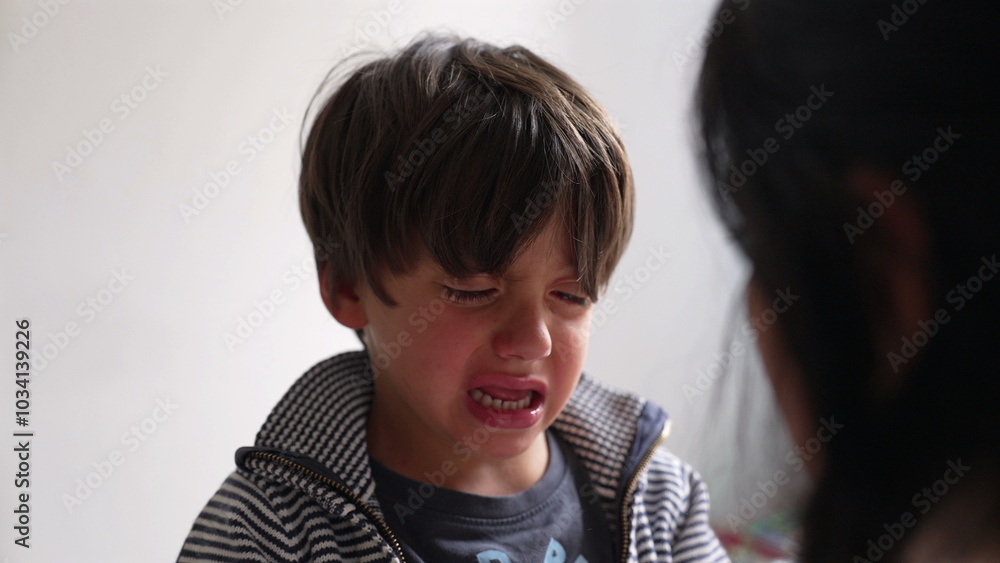 Young boy crying, visibly upset and distressed, while looking at mother ...