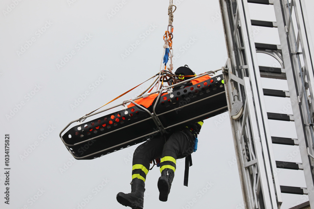 firefighter hanging from a rope lowers the stretcher with a badly ...
