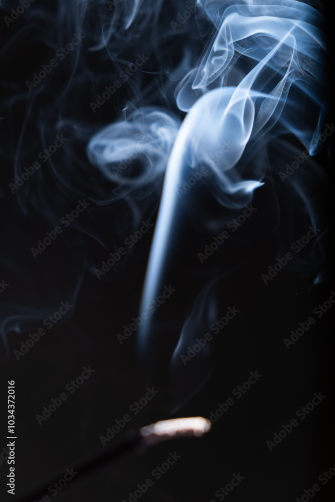 Wispy smoke curling upward from a burnt match against a dark backdrop ...