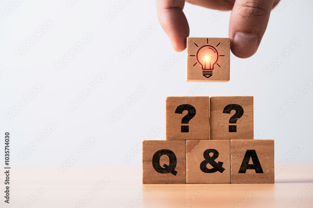 Hand putting glowing lightbulb on the top of wooden block cube on question mark and QA for ...