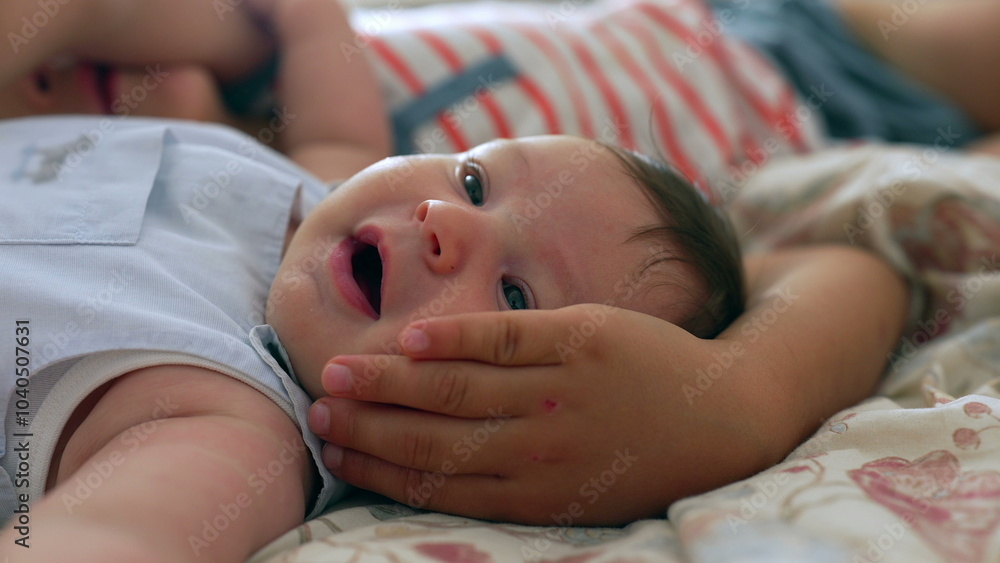 Baby lying on the bed with an older child's hand gently cupping the ...