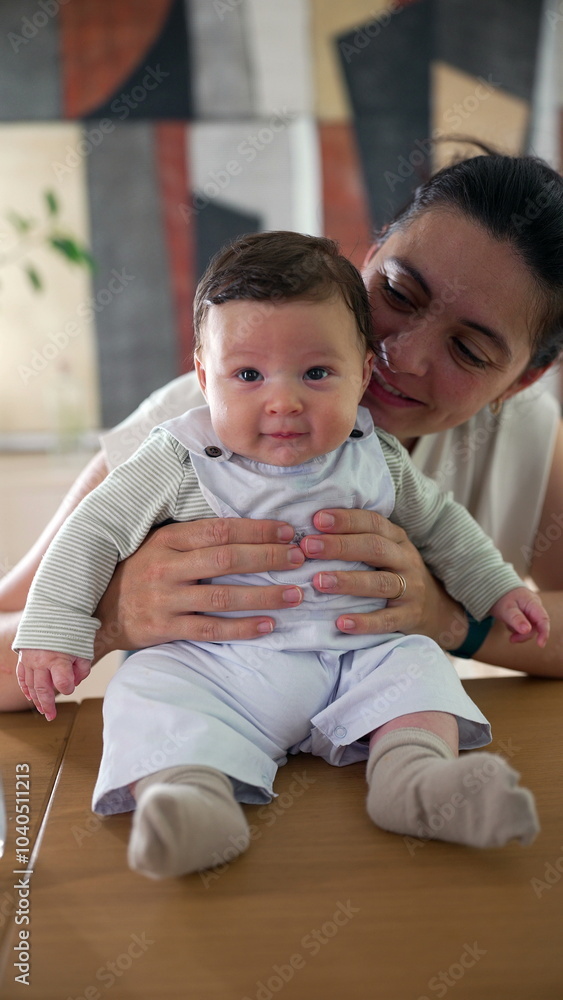 Baby sitting on a table, supported by the mother from behind. baby ...