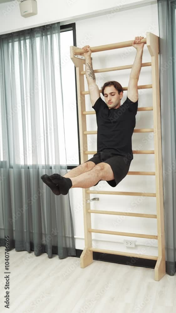 Happy man doing hanging leg raise exercise on wall bars to strengthen ...