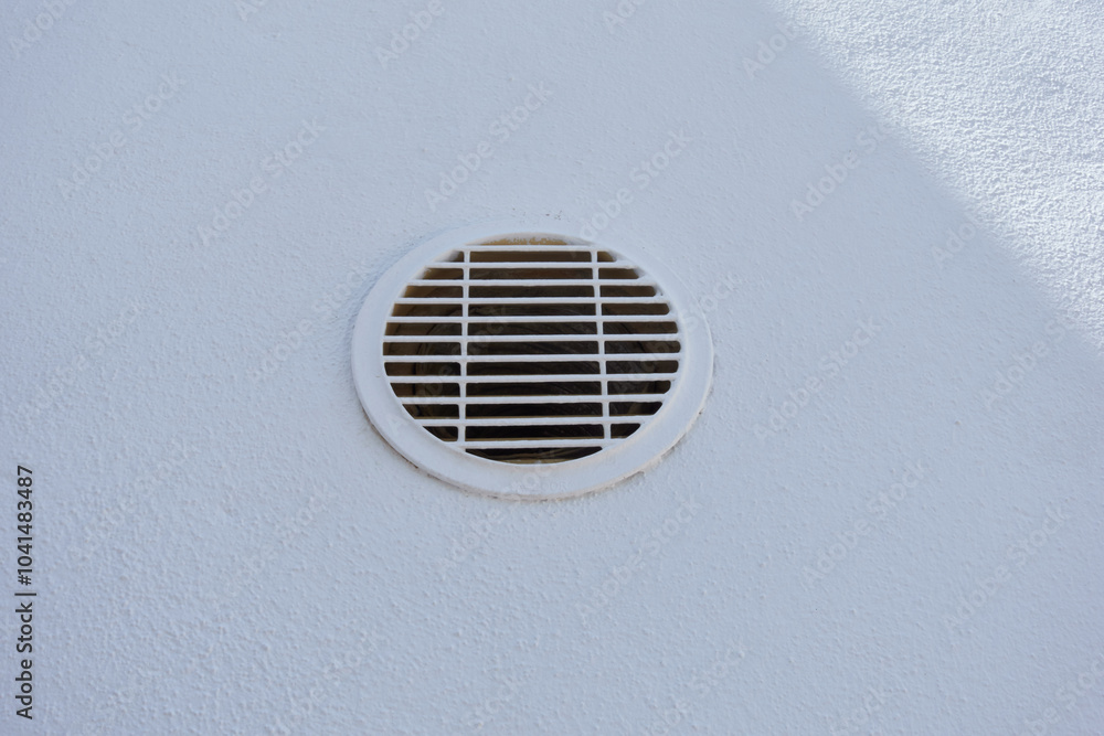 A circular white plastic air vent with horizontal slats on a textured ...