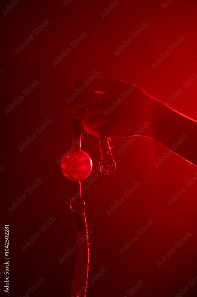 Red BDSM gag in the hands of a girl on a red background. BDSM is an ...