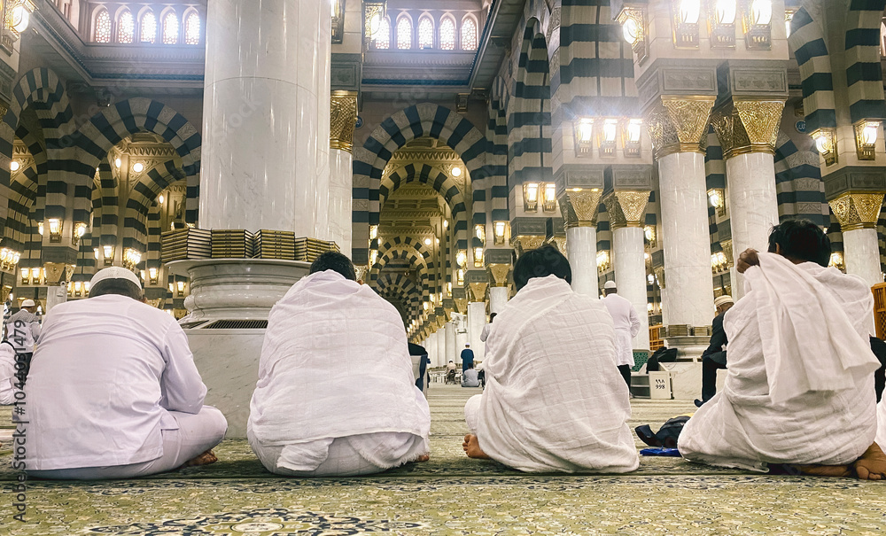Four people wearing white robes sitting inside the Al Masjid an Nabawi ...
