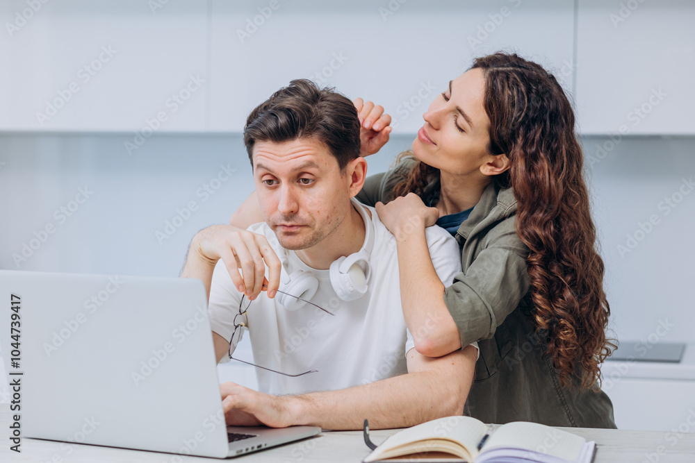 Couple in a cozy kitchen. Balancing work and affection while he focuses ...