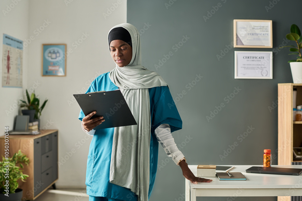 Muslim medical professional wearing scrubs and standing in modern ...