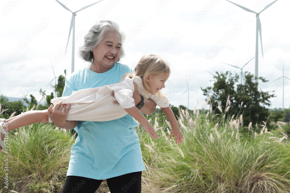 Grandma play with granddaughter at wind turbine farm. Asian elderly ...