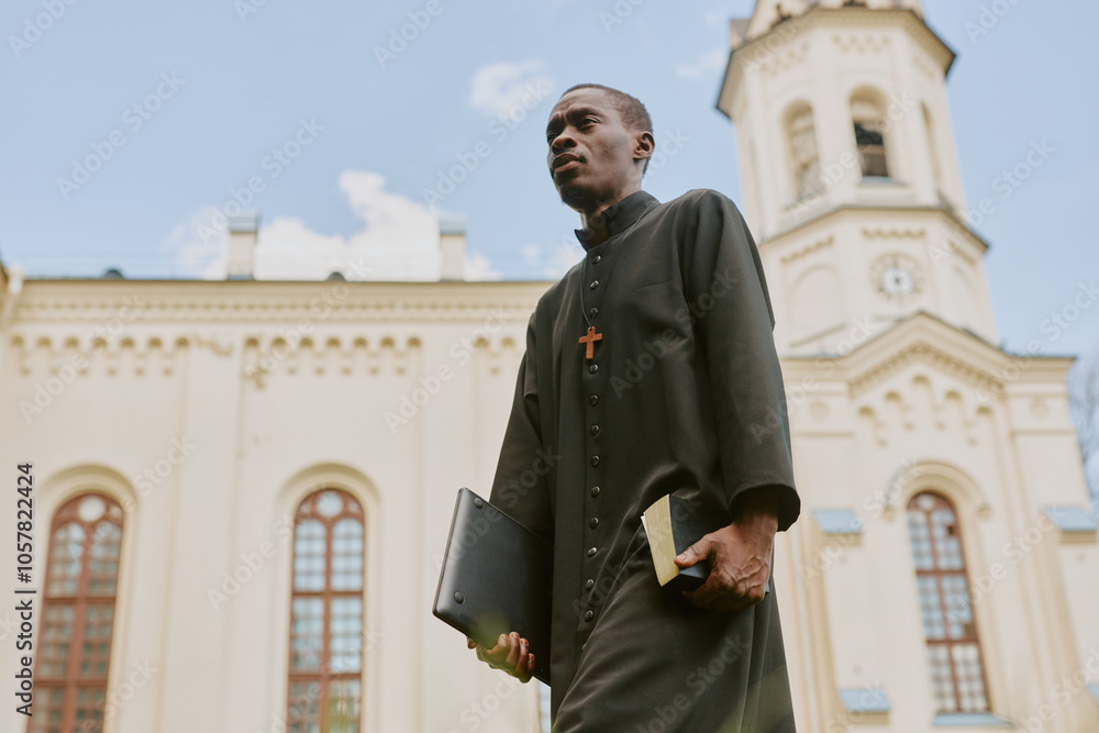 Low angle shot of African American priest in black robe with big wooden ...