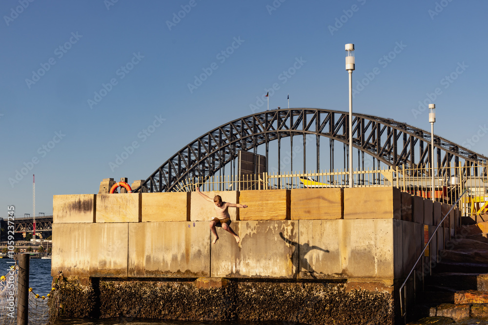 Kid jumping from ledge into water with Sydney Harbour Bridge in ...
