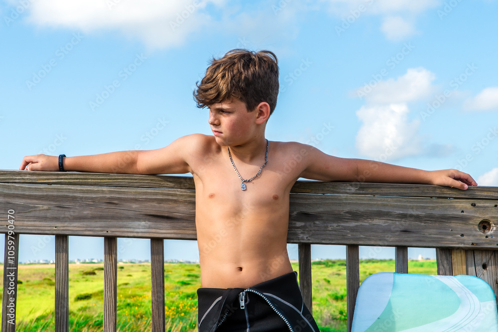 Young male surfer boy leaning on a wooden railing near the beach ...