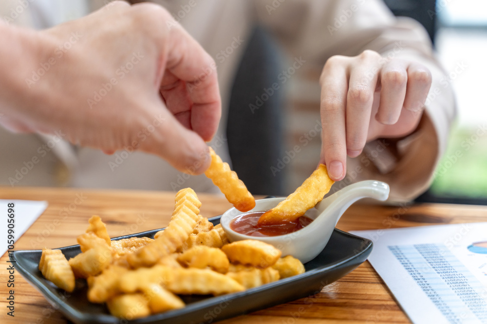Close up hands of two people holding a french fried dipping in ketchup ...