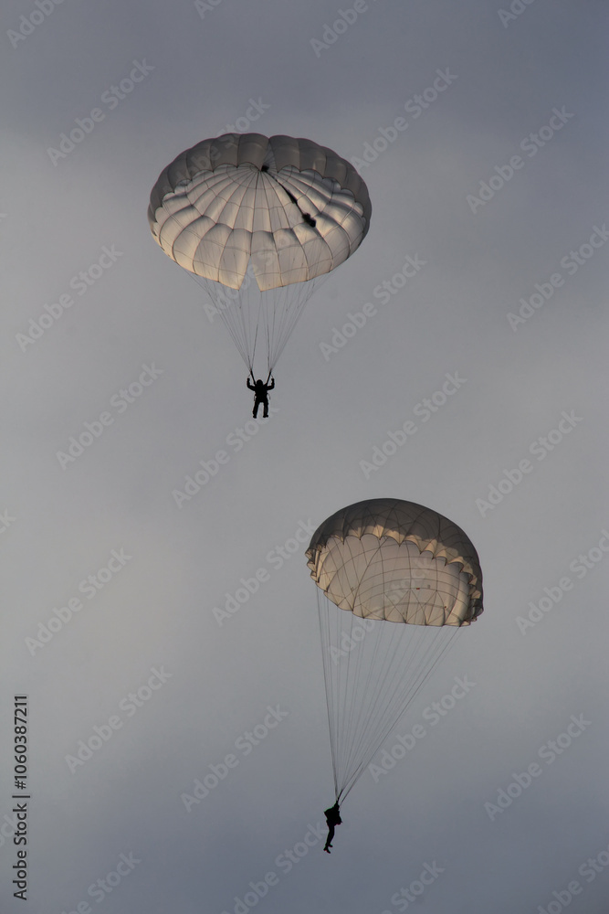 Two parachutists descending gracefully from the sky during a cloudy day ...