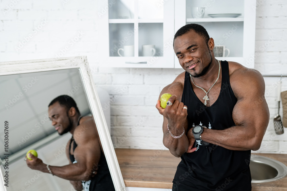 Bodybuilder holding an apple in a modern kitchen. A muscular man smiles ...