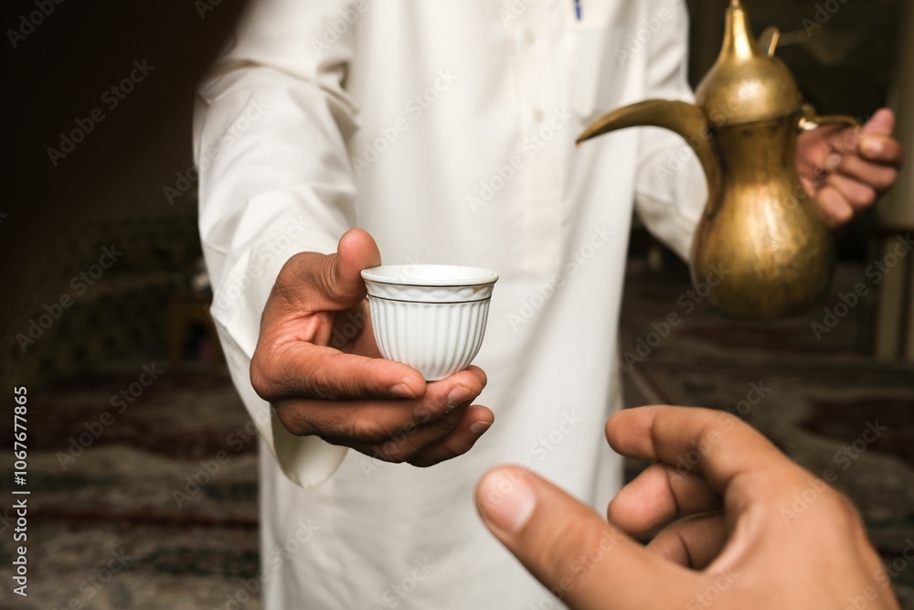 Middle Eastern man in traditional attire pouring Arabic coffee from a ...