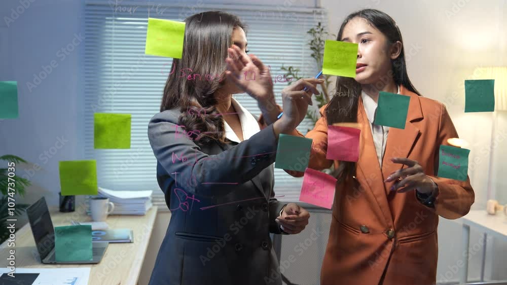 Two businesswomen are having a discussion while using sticky notes on a ...