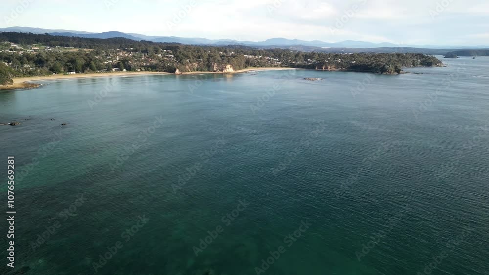 Drone scenery of blue waters and lush, forested shoreline with seafront ...