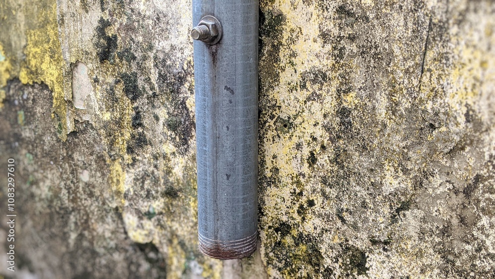 View of a metal pipe attached to a weathered wall. The pipe is rusted ...