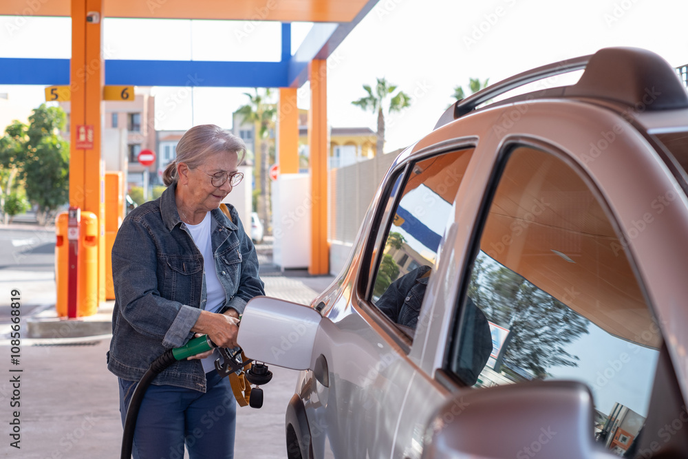 Mature modern woman fills up her car at self-service fuel pump in ...