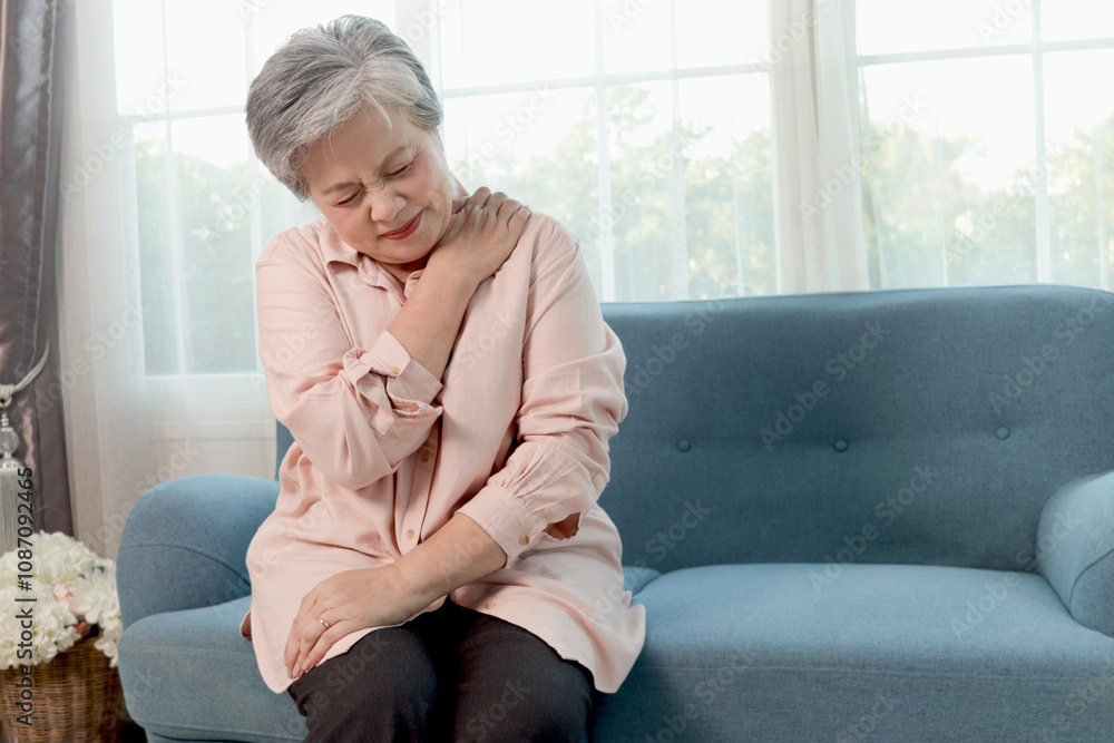 Asian senior woman suffering from shoulder pain while sitting on sofa ...