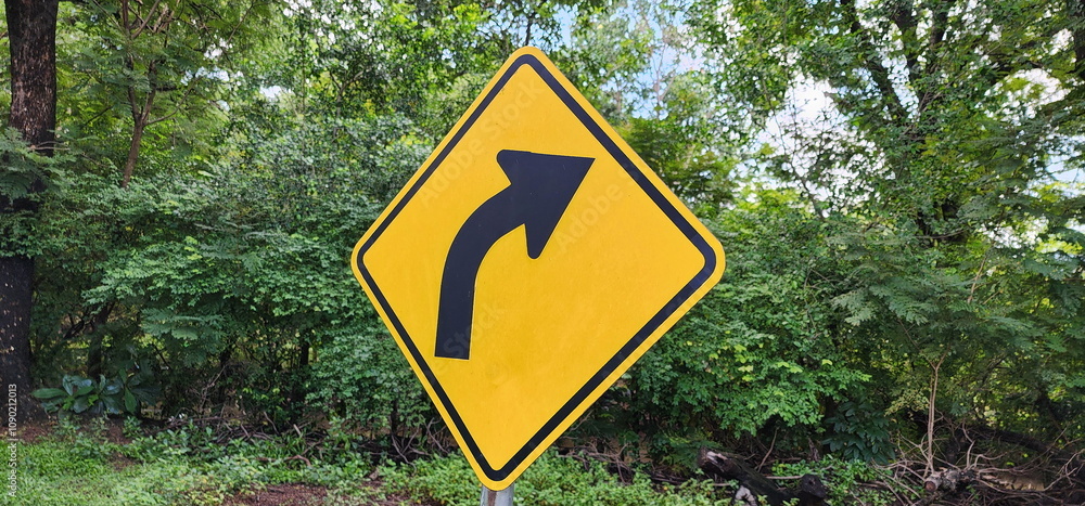 Right curve sign installed on the side of a rural road with a bush on ...