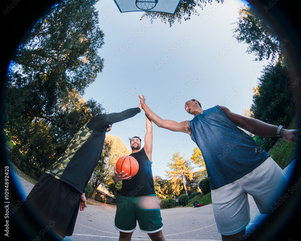 Three basketball players celebrate teamwork with a high five under the ...