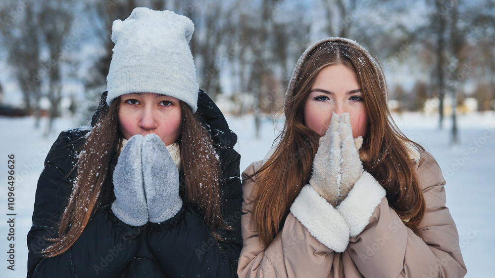 Two young girls in winter gear are breathing on their hands to keep ...