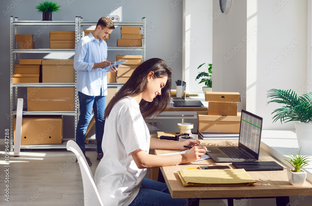 Female manager working on laptop at the desk in logistics or distribution center with male ...