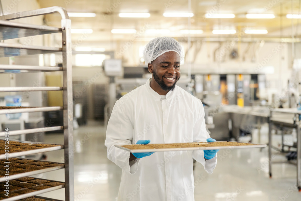 Smiling interracial migrant worker carrying tray with biscuits at food ...