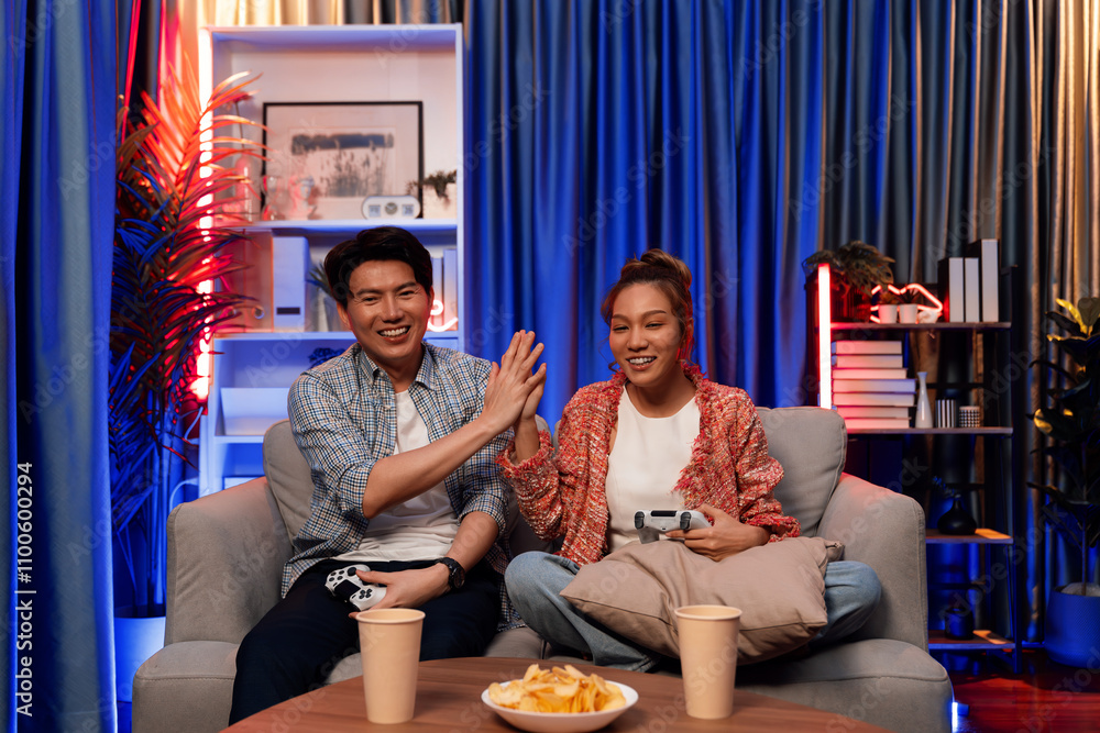 Couple gamer making high five holding joysticks be winner together complete level sitting sofa ...