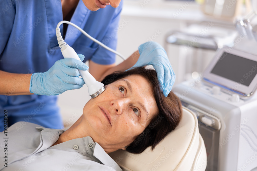 Elderly woman undergoing device-driven cosmetic facial treatment using ...