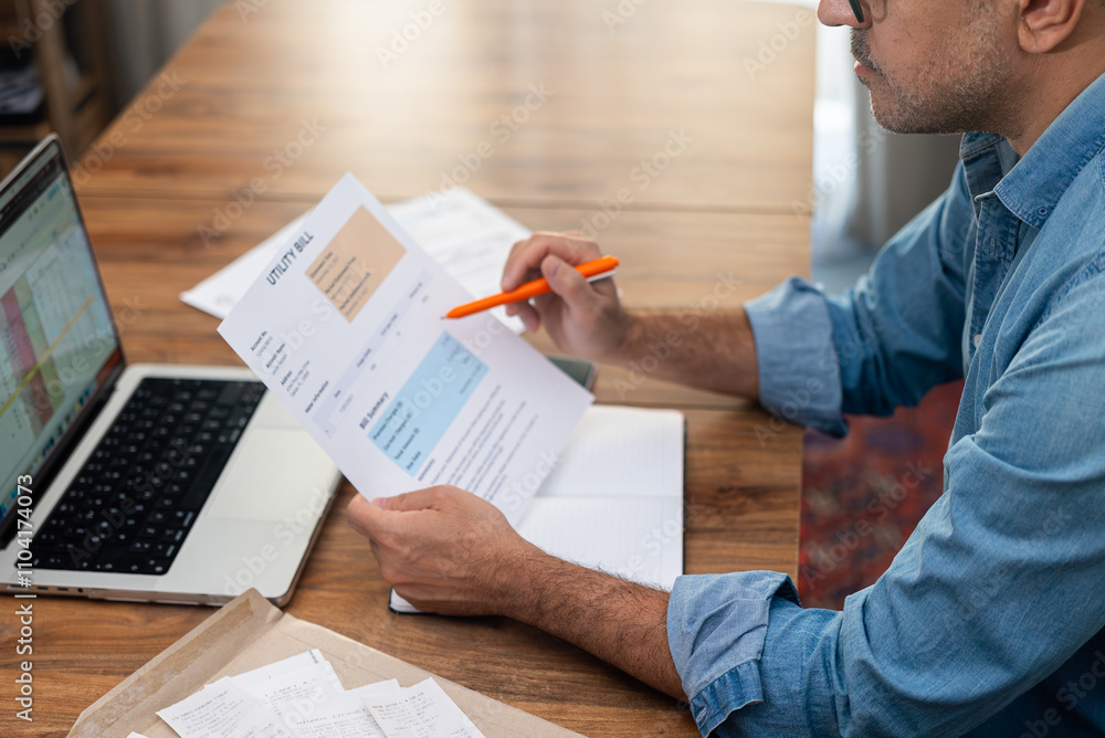 Man examining utility bill with pen and laptop at home office desk ...