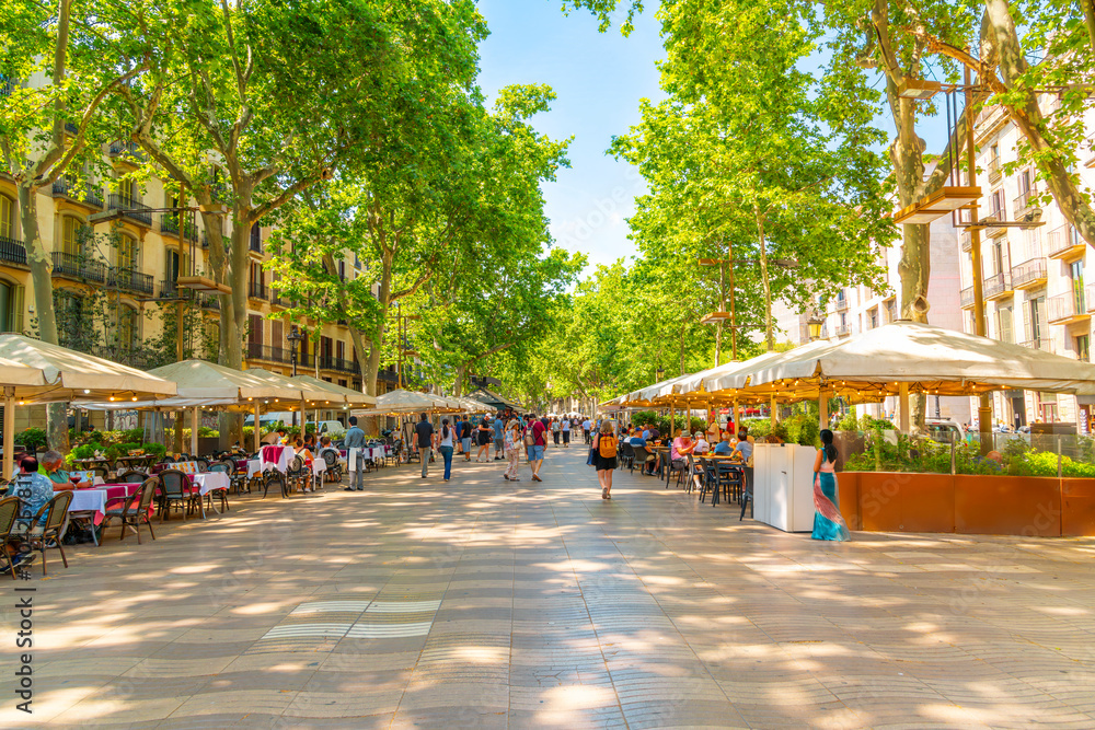 Tourists walk past sidewalk cafes on the famous La Rambla street ...