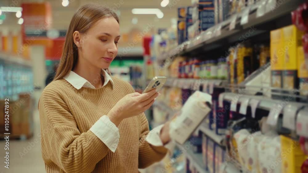 A woman stands in a brightly lit supermarket aisle scanning product labels with her smartphone ...