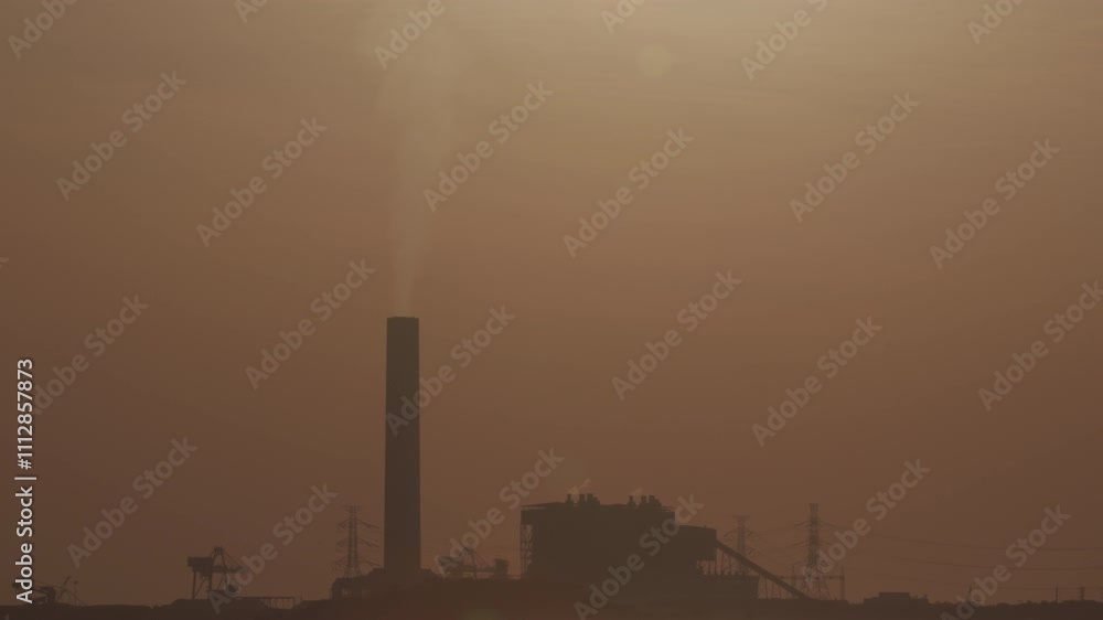 Smokestack emits smoke from power plant, silhouetted against sunset sky ...