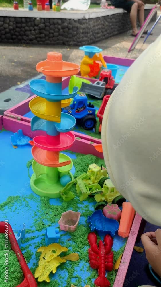 A child playing in a colorful sand play area with plastic toys ...