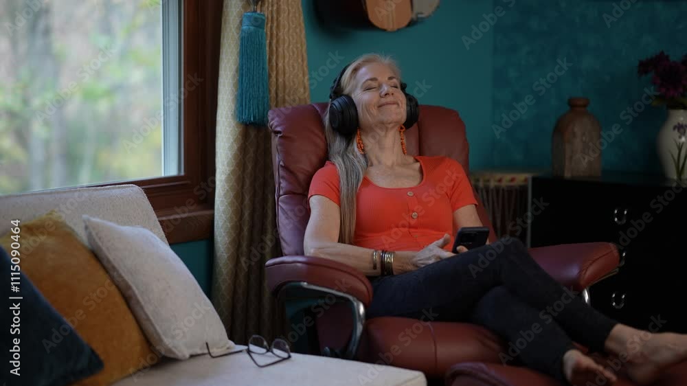 Mature woman wearing headphones and an orange shirt sits in a brown ...