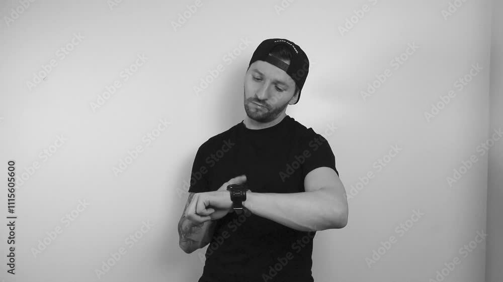 Grayscale footage of a tattooed man pointing and tapping his wristwatch ...