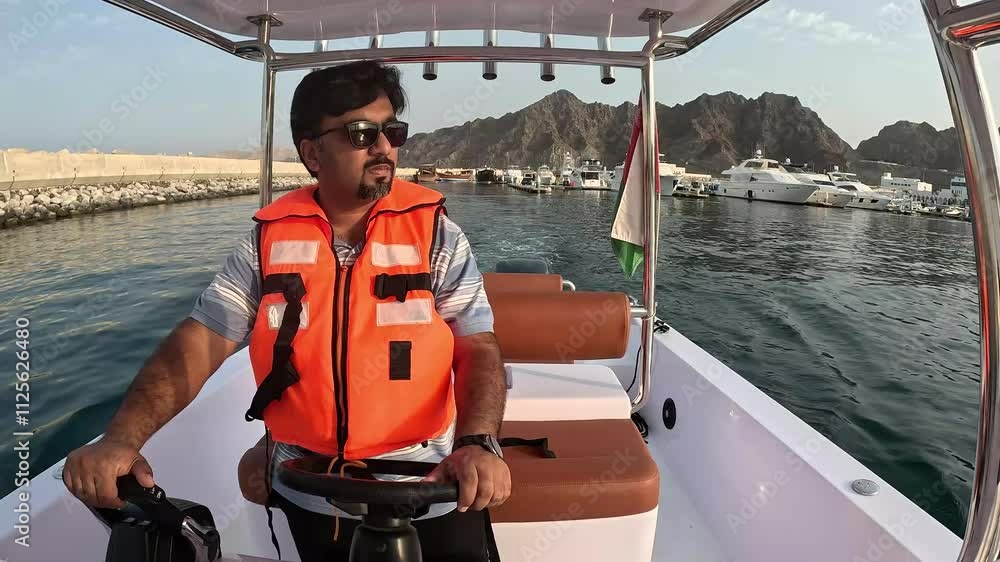 Close-shot of man in an orange life jacket steering a small boat ...