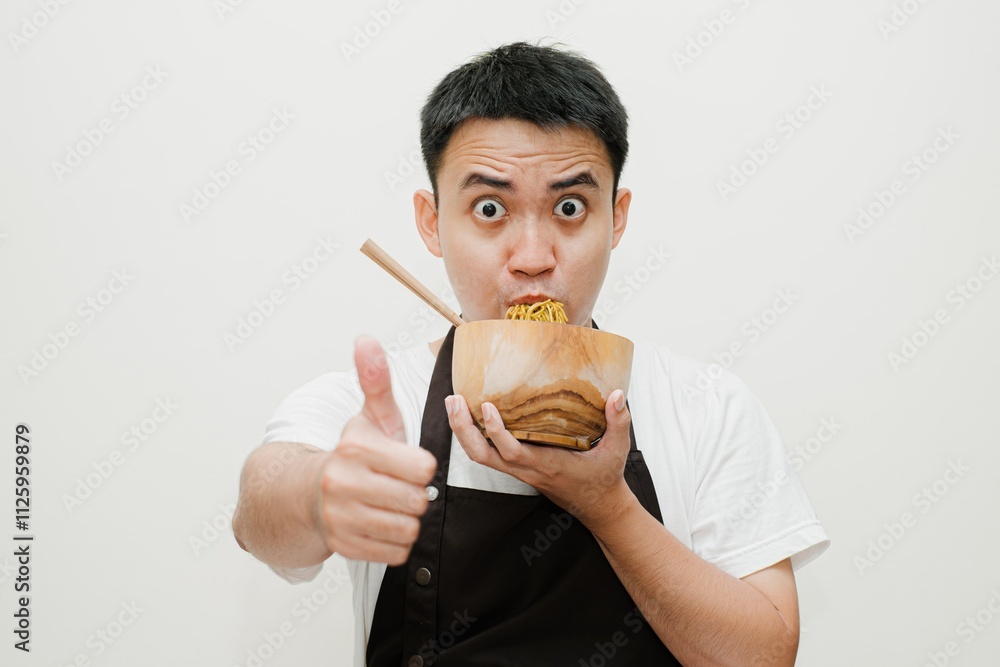 Shocked face of a young Asian chef giving thumb up while eating fried ...