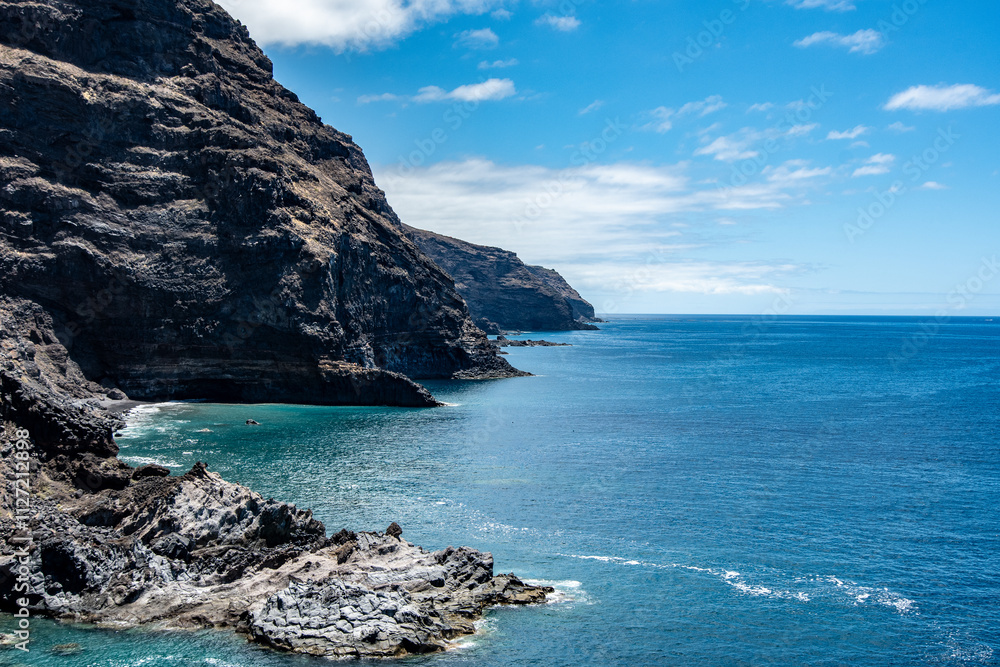 The image shows steep, rugged cliffs descending into a calm, blue ocean ...