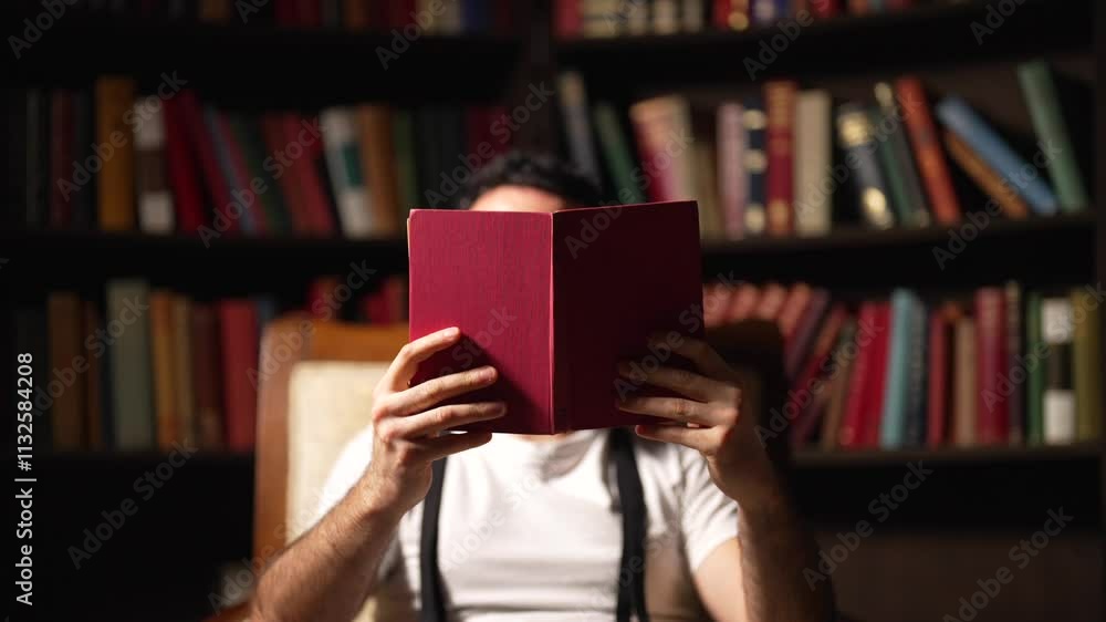 A young man opens a red book, face hidden; slow-motion captures him ...