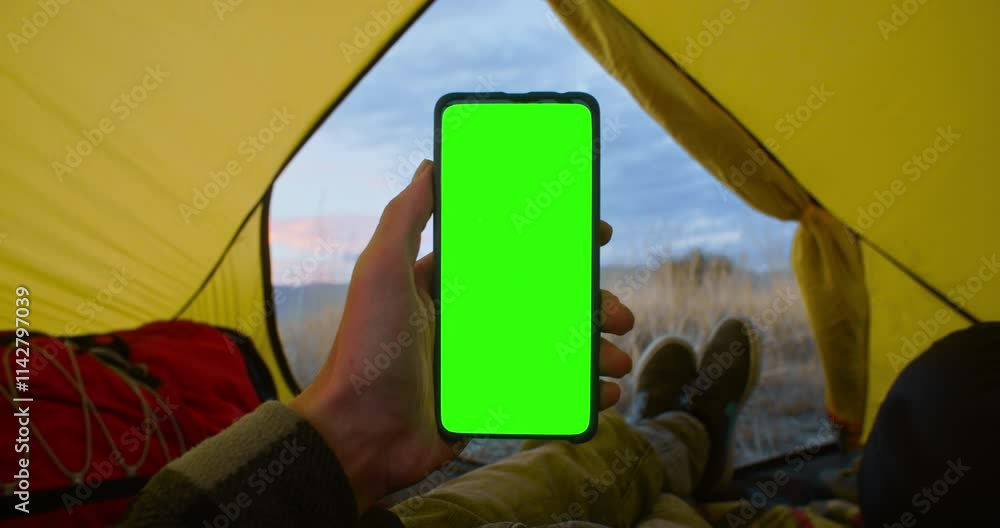 TAP. Person wearing a jacket is inside a cozy tent holding mobile phone ...