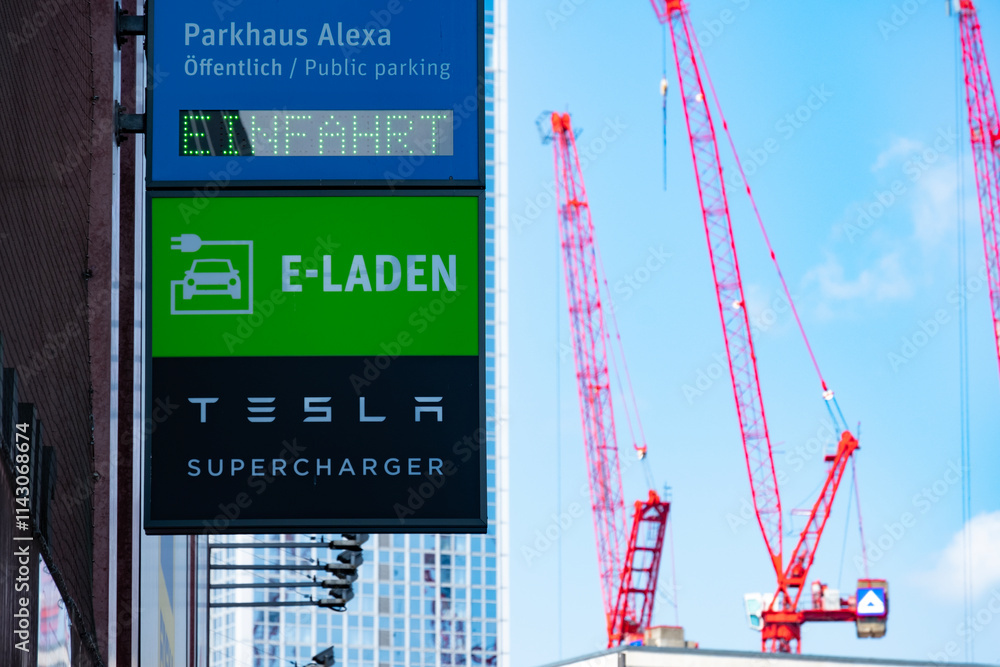 Tesla Supercharger sign stands tall against backdrop urban construction ...