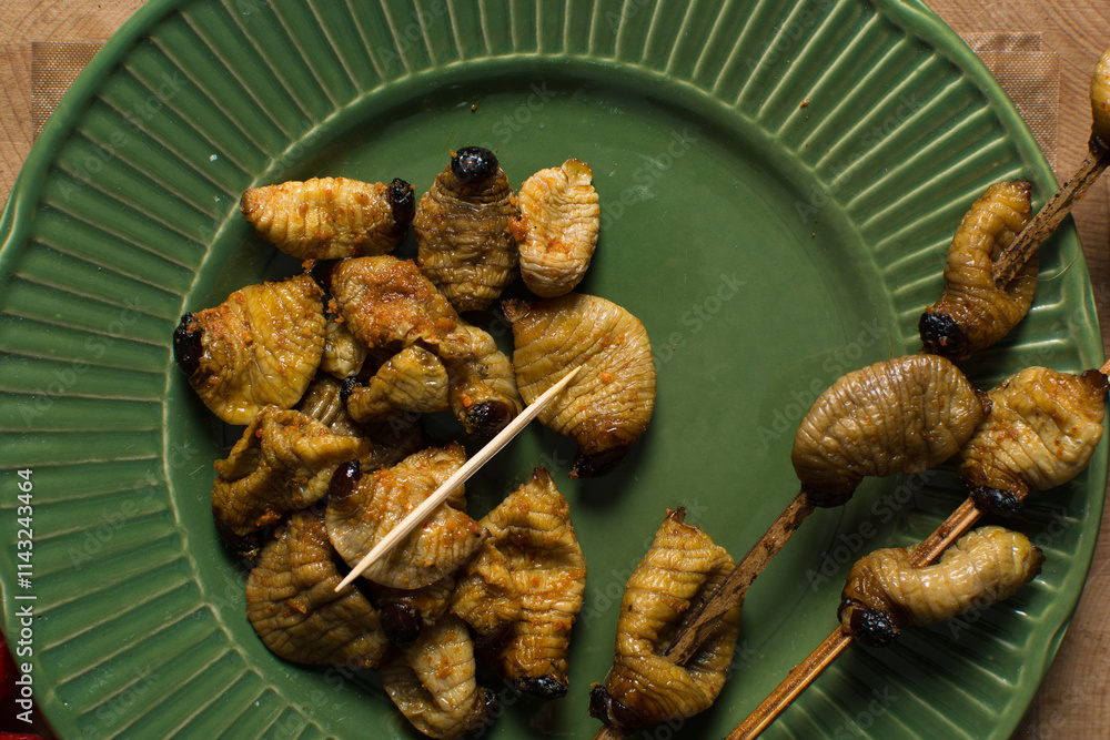 Overhead view of roasted sago worms on a green plate, top view of palm ...