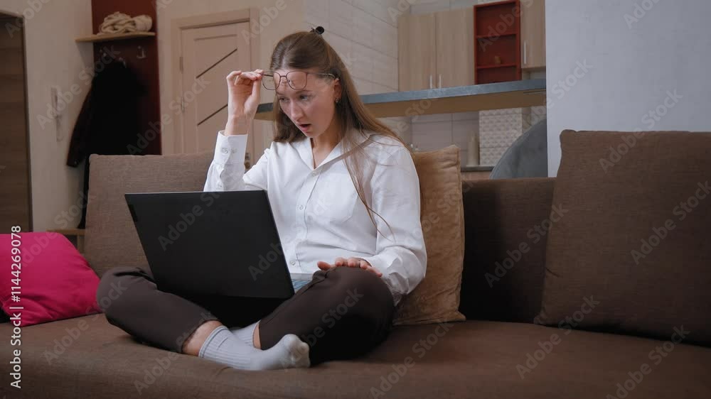 Young woman adjusting her glasses while frowning at laptop screen ...