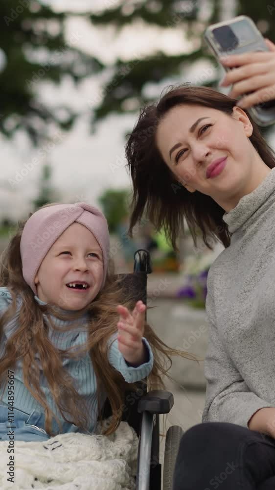 Mamma takes selfies while little girl with disability making funny gestures with hands. Woman ...
