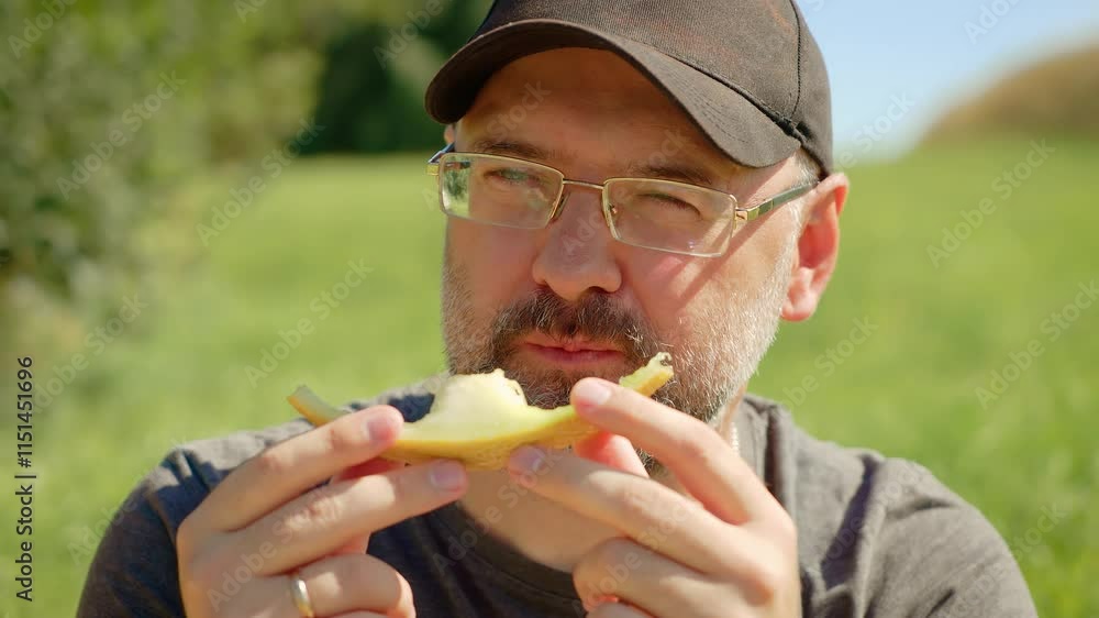 Bearded man eating juicy melon with focused expression and relaxed ...
