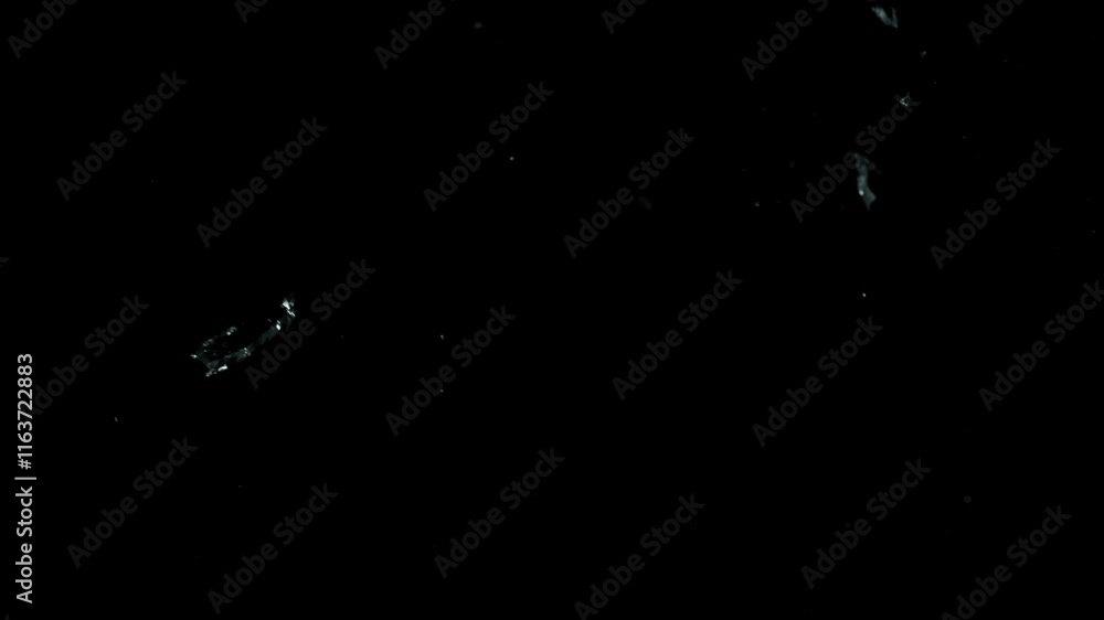 Shattered glass fragments fly through the air, set against stark black ...